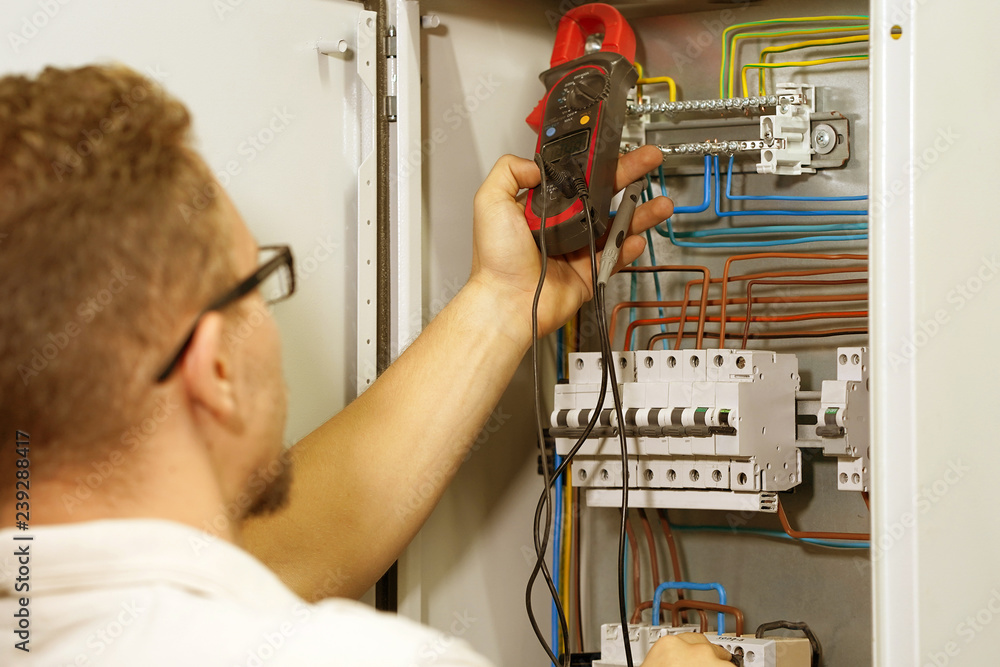 Electrician male measures voltage with multimeter in electrical cabinet ...