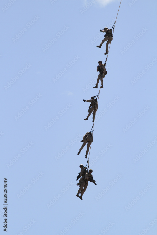 Military men flying through the air hanging on a rope from a helicopter ...