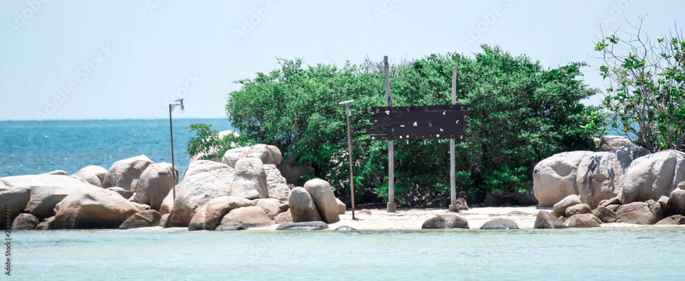 Small island with big rocks and wooden handmade blank sinage in a beach ...