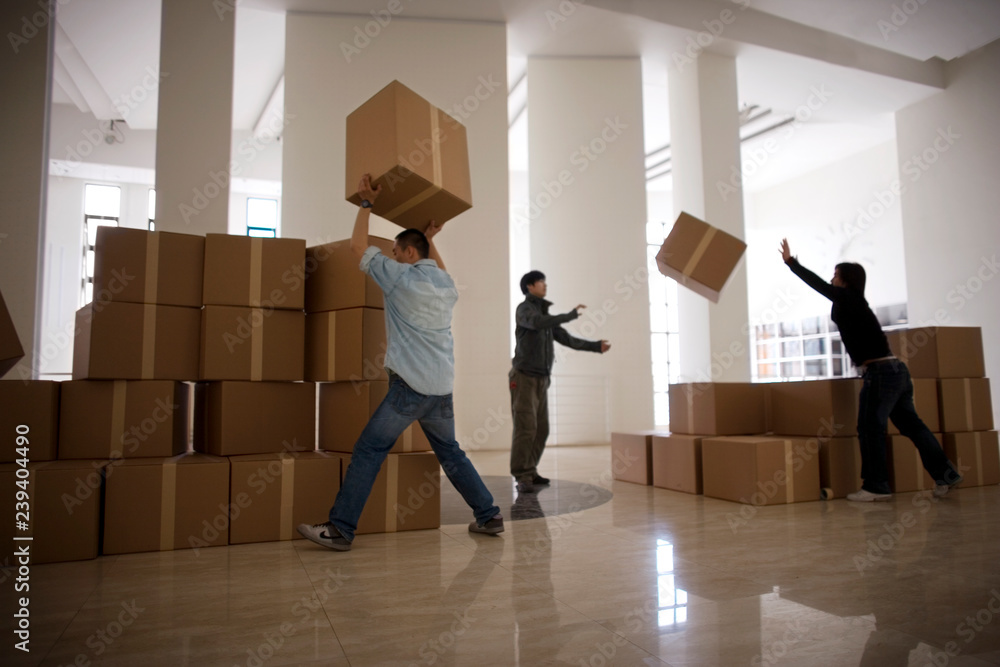Three young adult men stacking boxes to carry. Stock Photo | Adobe Stock