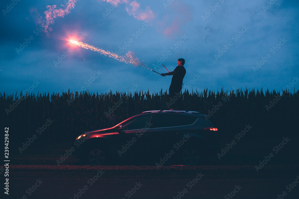A man shoots fireworks off of the roof of his SUV car in a corn field ...