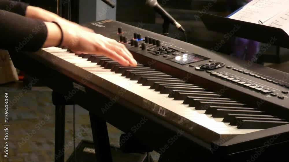Hands playing a keyboard on a stage from a chord chart in a dark room ...