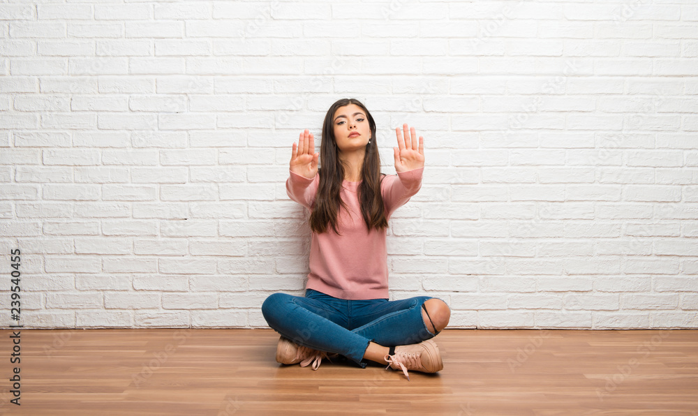 Teenager girl sitting on the floor in a room making stop gesture for ...