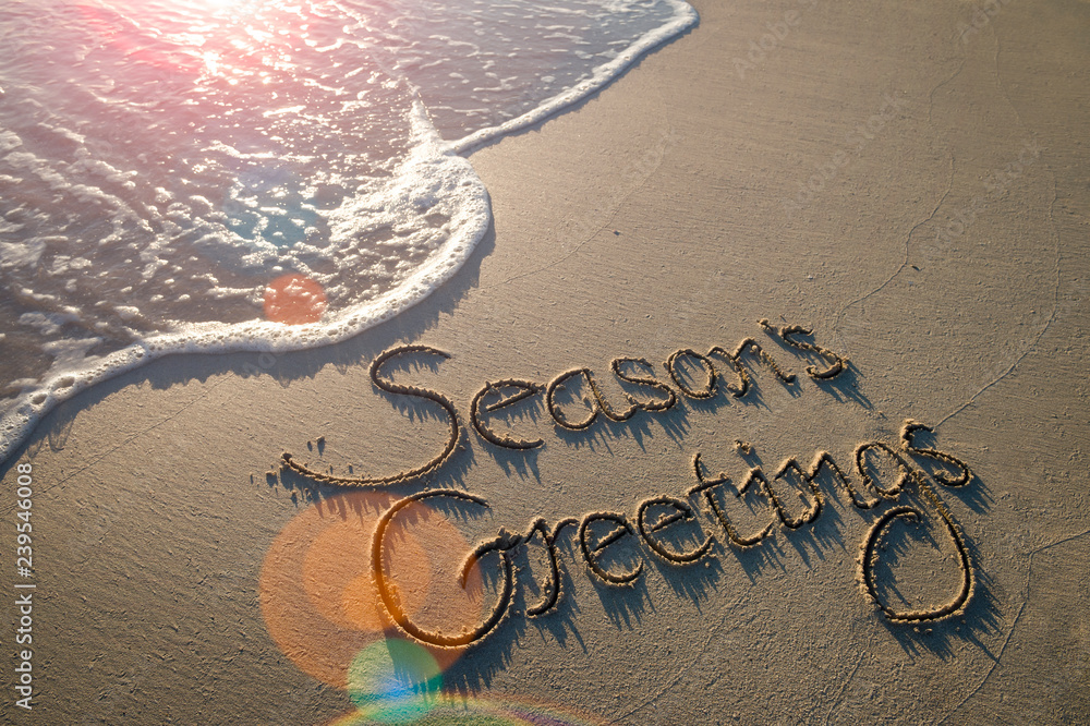 Season's Greetings message handwritten in smooth sand with an oncoming ...