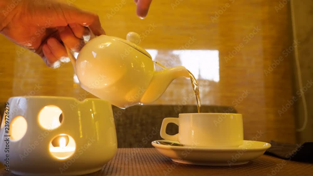 Male hand taking kettle standing on candle and pouring hot red tea in ...