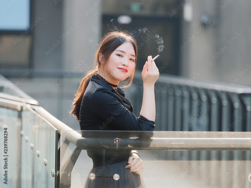 Portrait of beautiful Chinese girl in black dress smoking a cigarette ...
