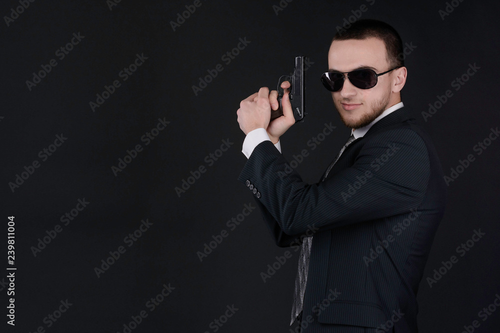 Man in black suit and sunglasses hold a gun in his hand. Prepearing to ...