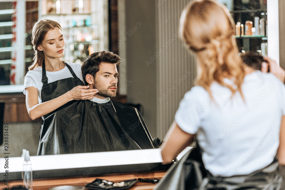 reflection in mirror of hairdresser doing hairstyle to handsome client ...