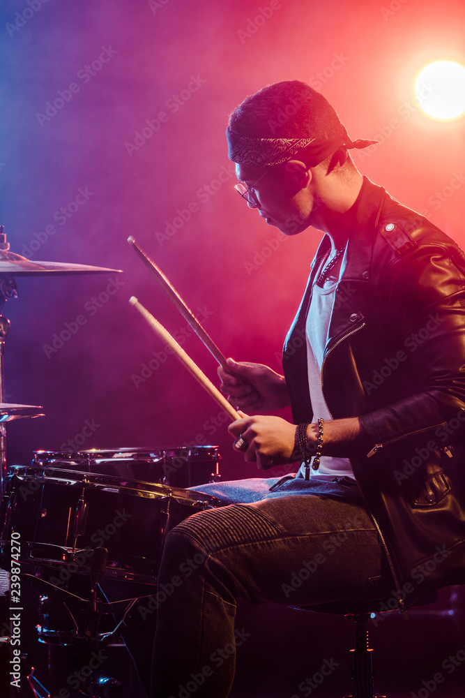 side view of male musician in leather jacket playing drums during rock ...