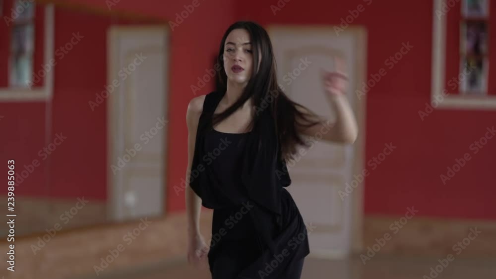 Attractive young slim girl with dark hair, in black top and leggings is ...