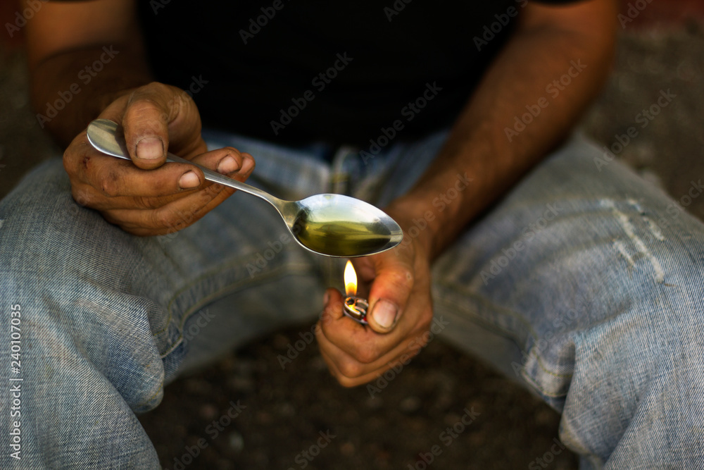 Drug addicted man in jeans sitting on the ground with syringe in his ...