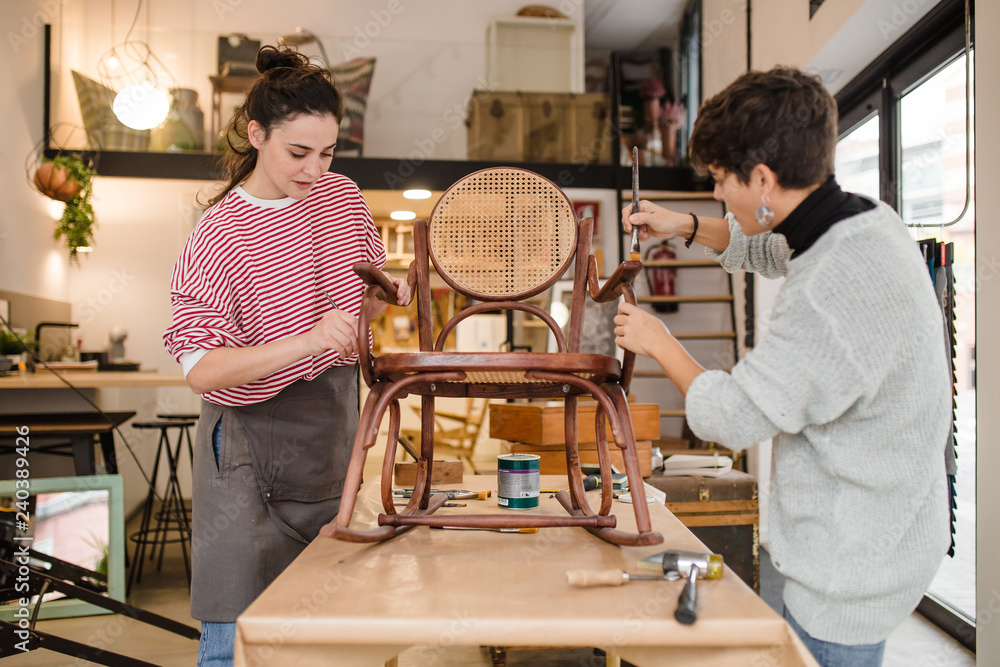 Side view of two women partners restoring and varnishing an old wooden ...