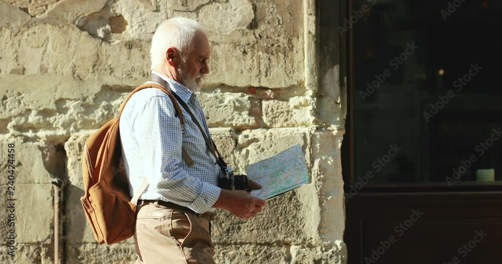 Caucasian old man walking as a tourist in the historic town with a map ...