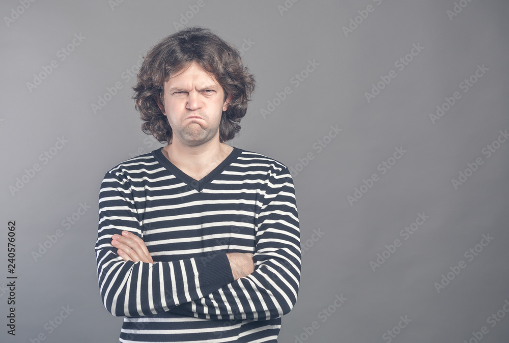 Angry young man in striped sweater puffed up his cheeks and crossed ...