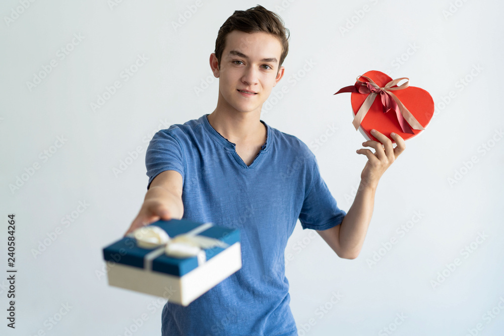 Smiling teen boy giving gift box to viewer. Young man standing, holding ...