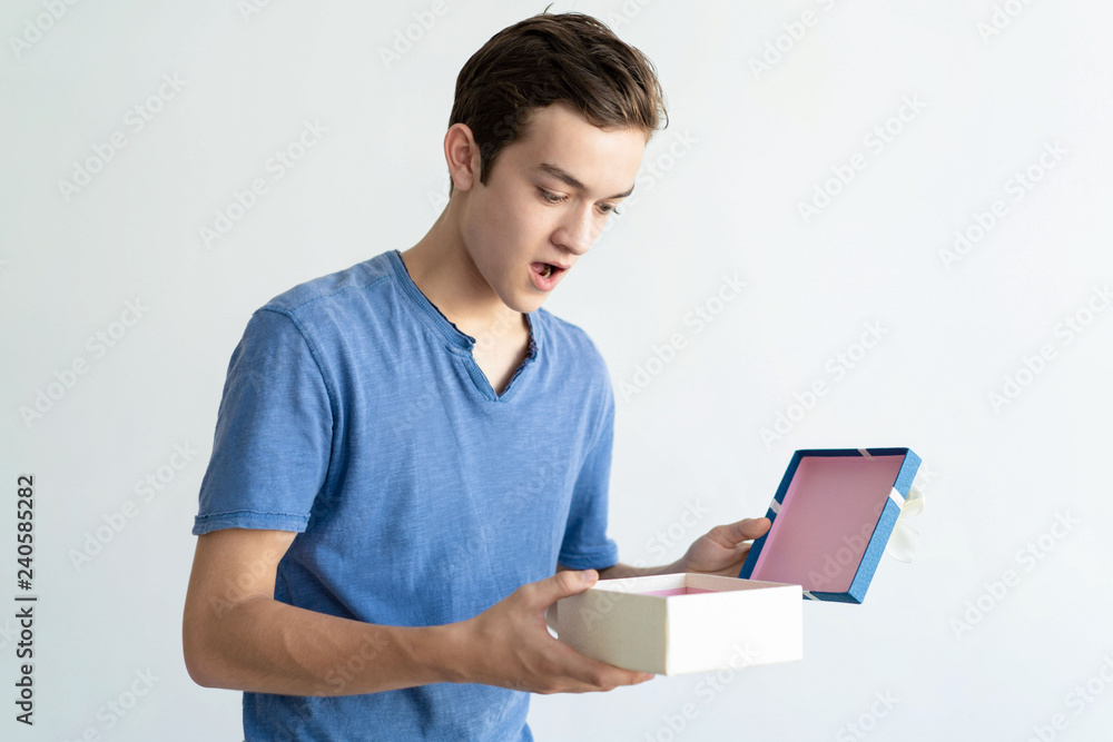 Surprised teen boy looking into open gift box. Young man standing and ...