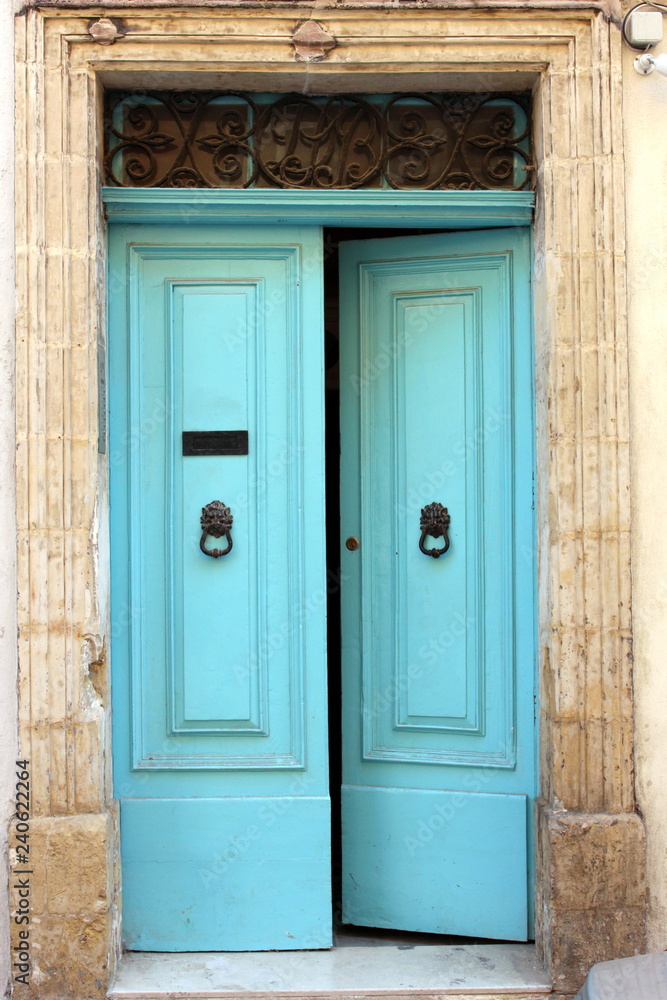 Turquoise blue doors, slightly ajar, with black iron metalwork knocker ...