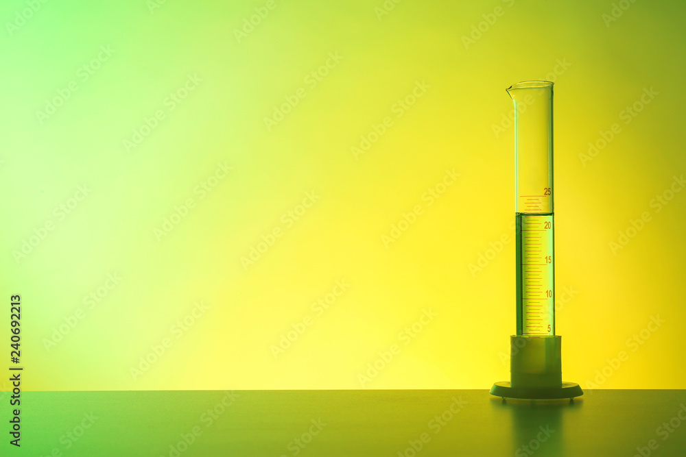 Graduated cylinder with liquid on table against color background ...