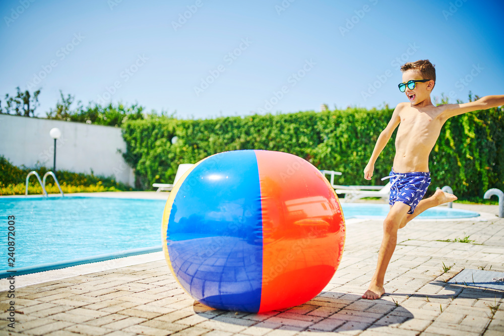 Shirtless boy playing with beach ball at poolside Stock Photo | Adobe Stock