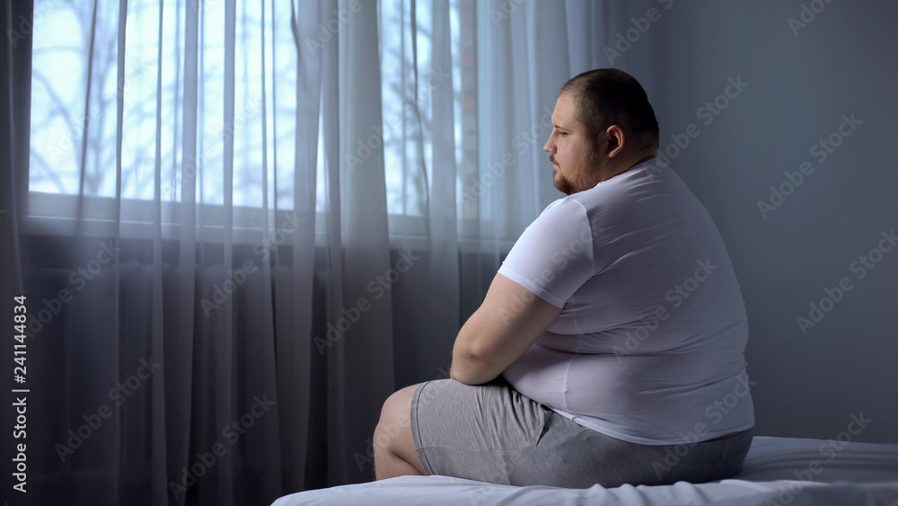Depressed fat man sitting on bed at home, worried about overweight ...