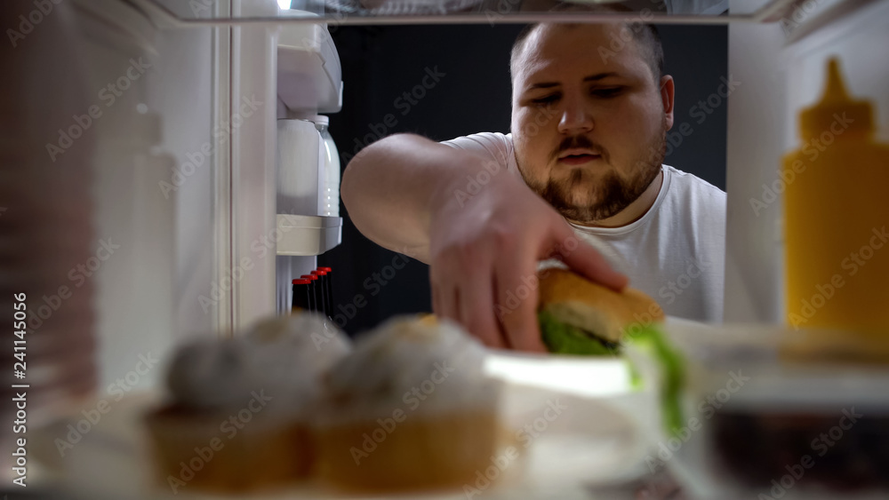 Obese hungry man taking hamburger from fridge, diet failure, unhealthy ...