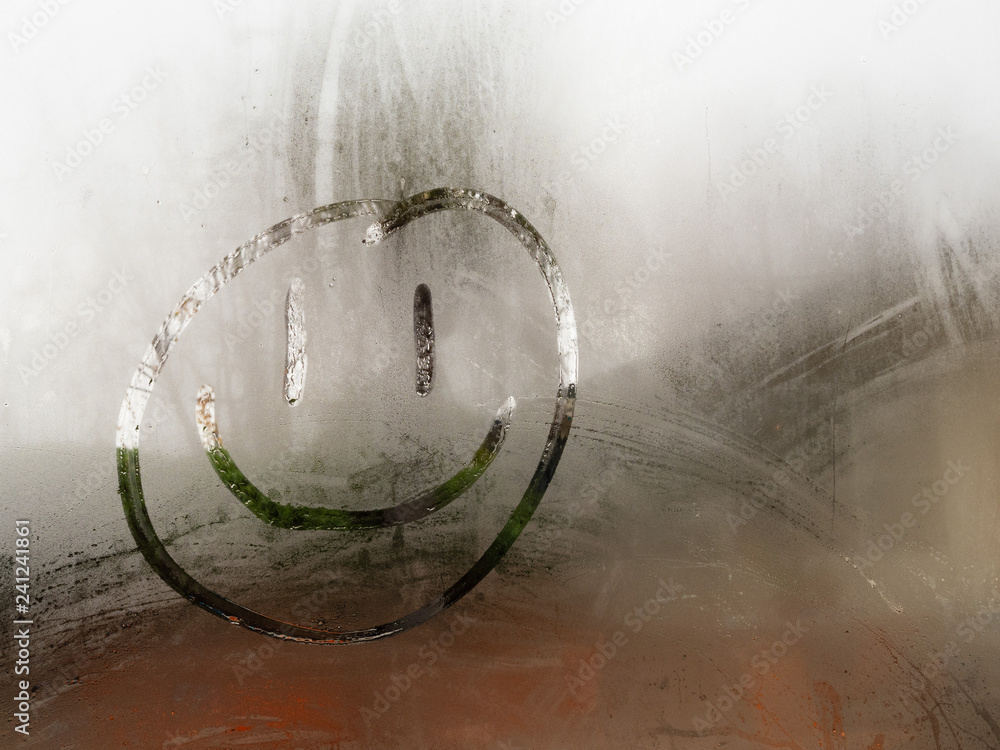 Cartoon happy smiley face drawn on a condensation covered window during ...