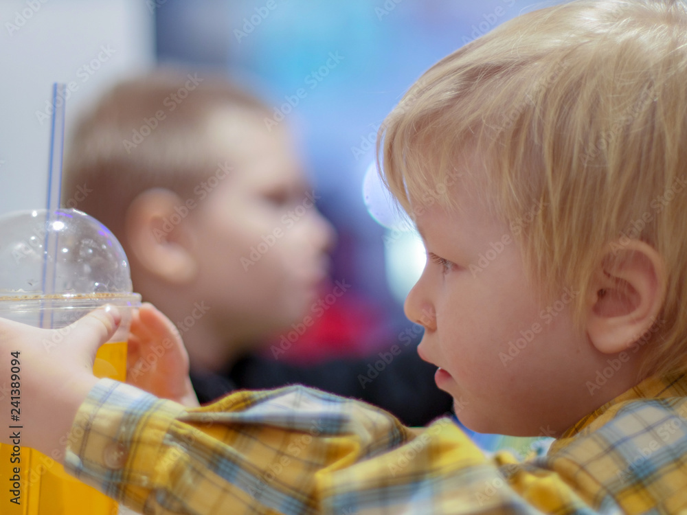 Cute little blond child drinks carbonated drink through straw and eats ...