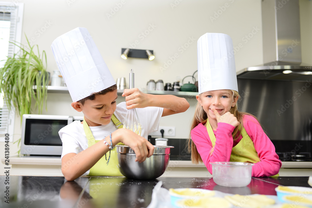 beautiful young happy kids boy and girl cooking and baking a cake in ...