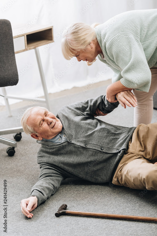 old woman helping to stand up husband who falled down on floor with ...