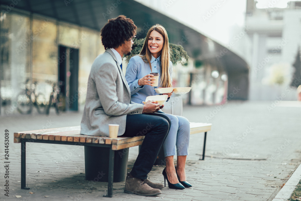 Smiling businessmen with sandwiches sitting in front of the office ...