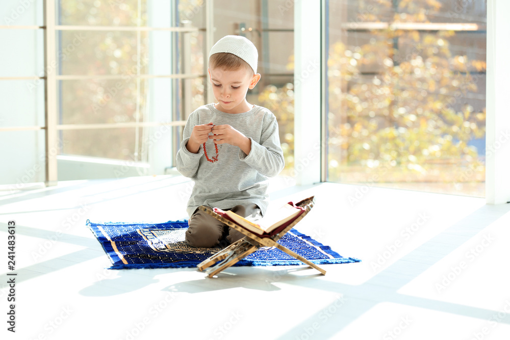 Little Muslim boy with misbaha and Koran praying on rug indoors Stock ...