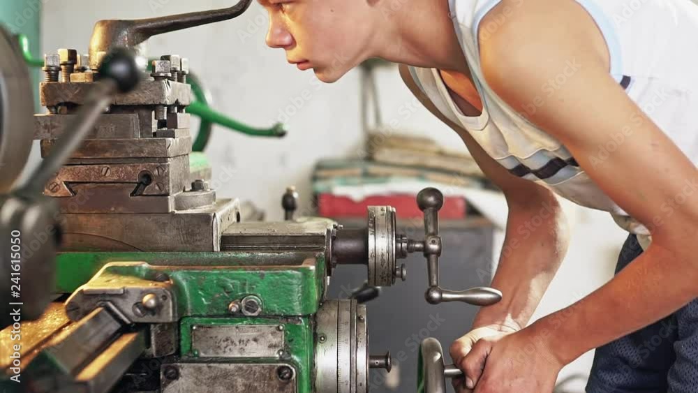 Young teenage boy using industrial lathe machine. A close up of a young ...