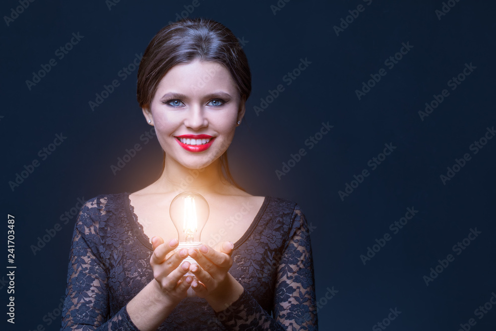 girl smiles and holds a glowing bulb in her hands. in the dark cold ...
