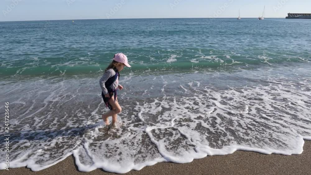 Barefoot little girl kid joyfully walking shallow waterline of Malaga ...