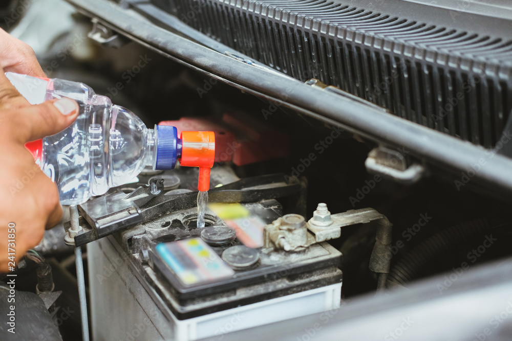 mechanic pouring distilled water to fill car battery in automobile ...