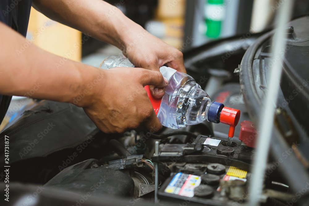 mechanic pouring distilled water to fill car battery in automobile ...