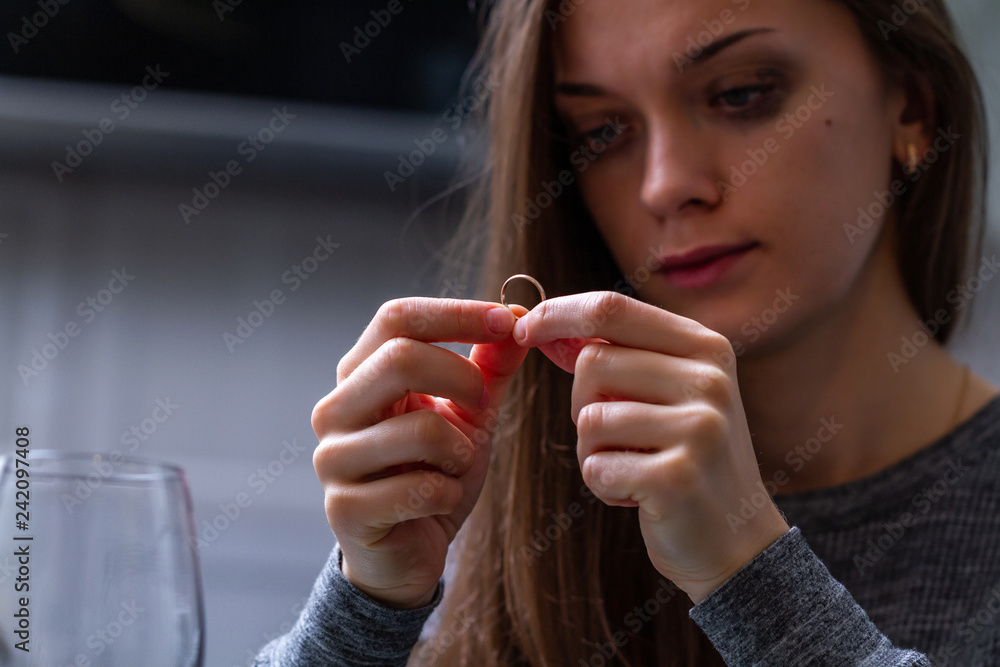 Crying, divorced woman holding a wedding ring and drinking a glass of ...