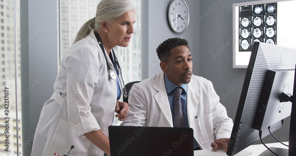 Portrait of millennial black doctor using computer while senior ...