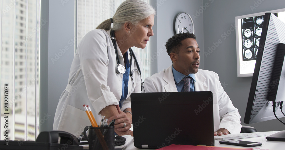 Foto de Portrait of millennial black doctor using computer while senior ...