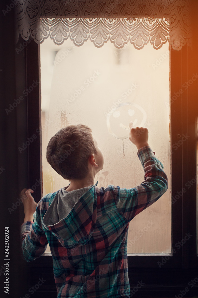 Back view of little child drawning smile on fogged glass looking ...