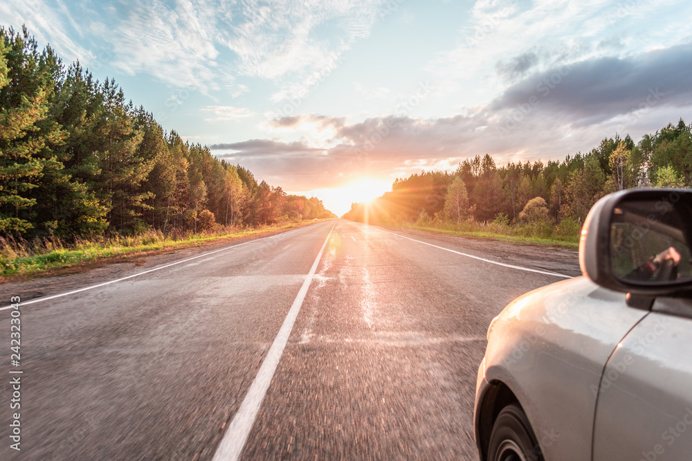 The car moves on the road through the woods during sunset. Photo taken ...