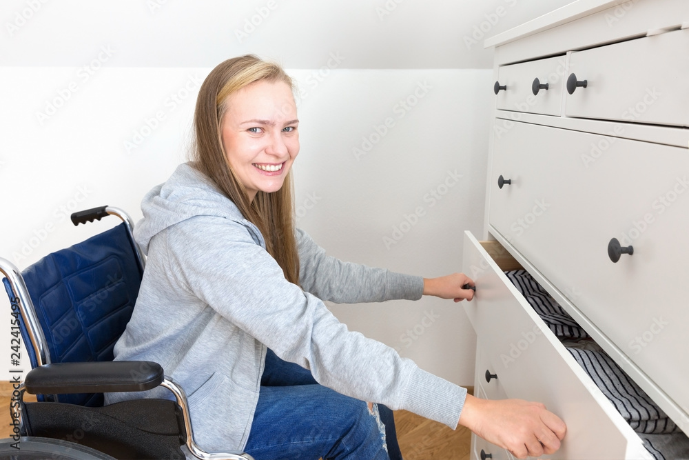 Young disabled woman in wheelchair opens drawers in the dresser. Stock ...