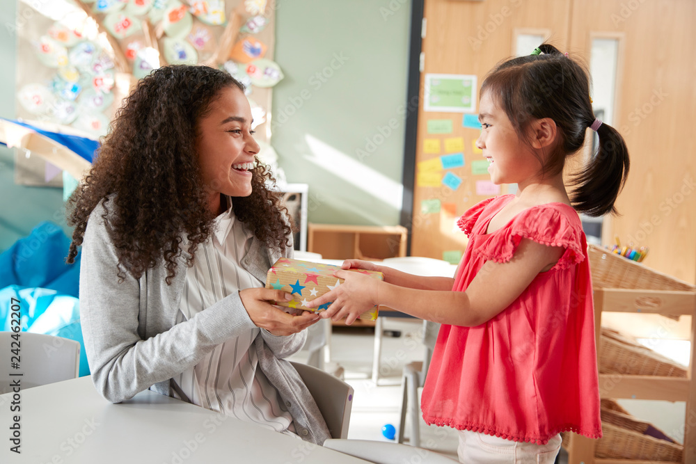 Kindergarten schoolgirl giving a gift to her female teacher in a ...