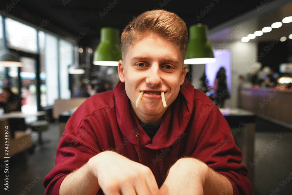 Funny young man with French fries instead of teeth, sits at the ...