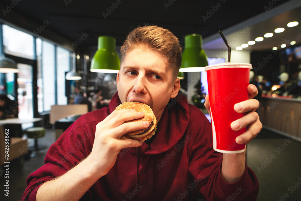 Funny student eating burger in fast food restaurants, holding a glass ...