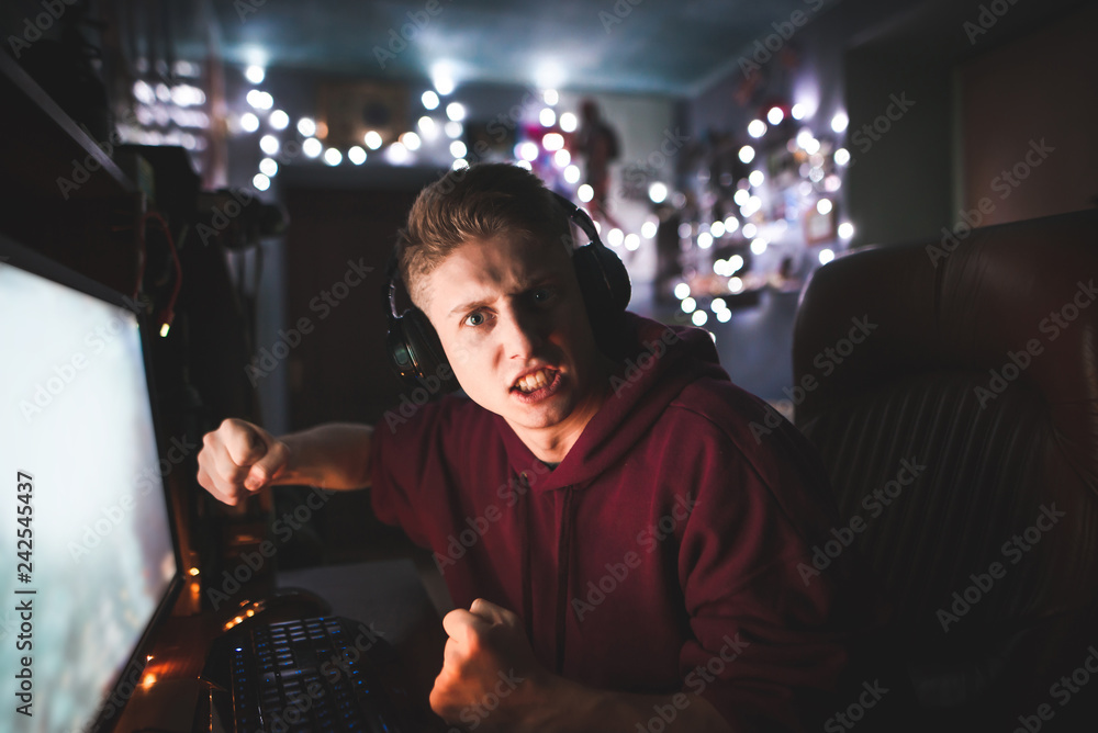 Angry young gamer in headphones plays video games at home on a computer ...