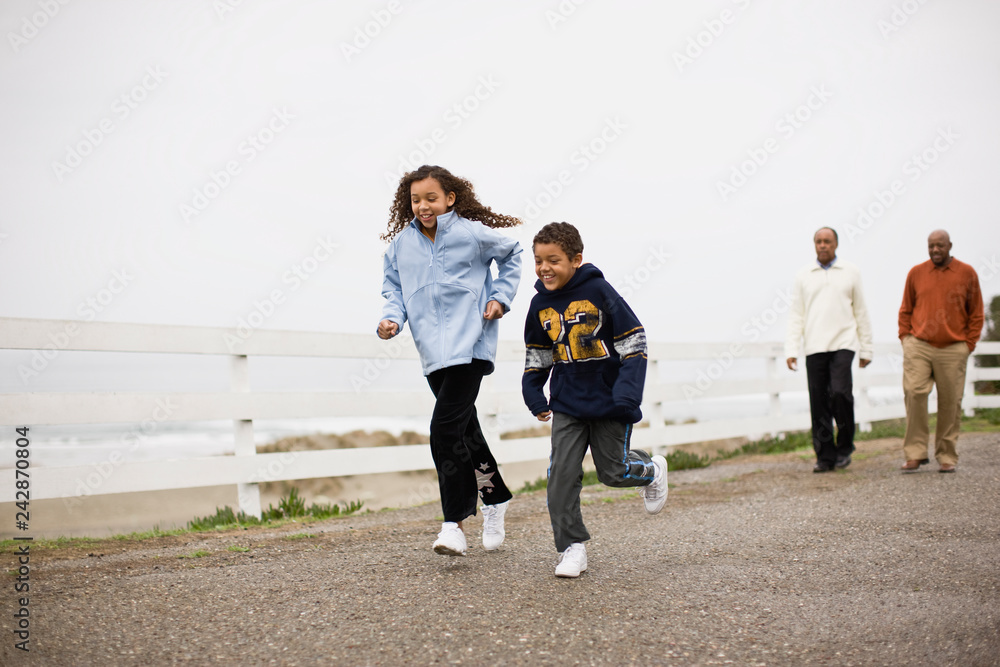Brother and sister running ahead of their father and grandfather on a ...