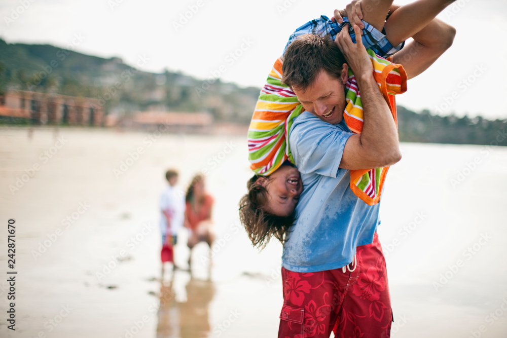 Father carrying his son upside down, over his shoulder at the beach ...