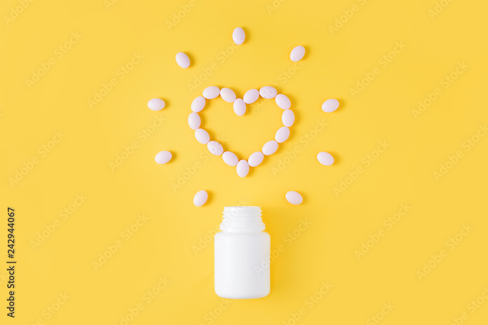 Pills in shape of heart dropped from bottle on yellow background. Flat ...