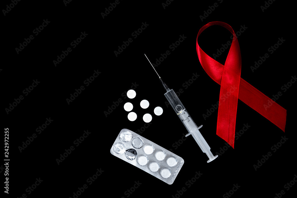 Red ribbon, pills and syringe on black background. HIV, AIDS, substance ...